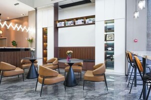 Um saguão de hotel moderno, com balcão de recepção, área de estar e uma parede decorativa com quadros.