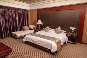 Quarto de hotel com uma cama grande, uma cama menor, uma escrivaninha e uma mesa de cabeceira.