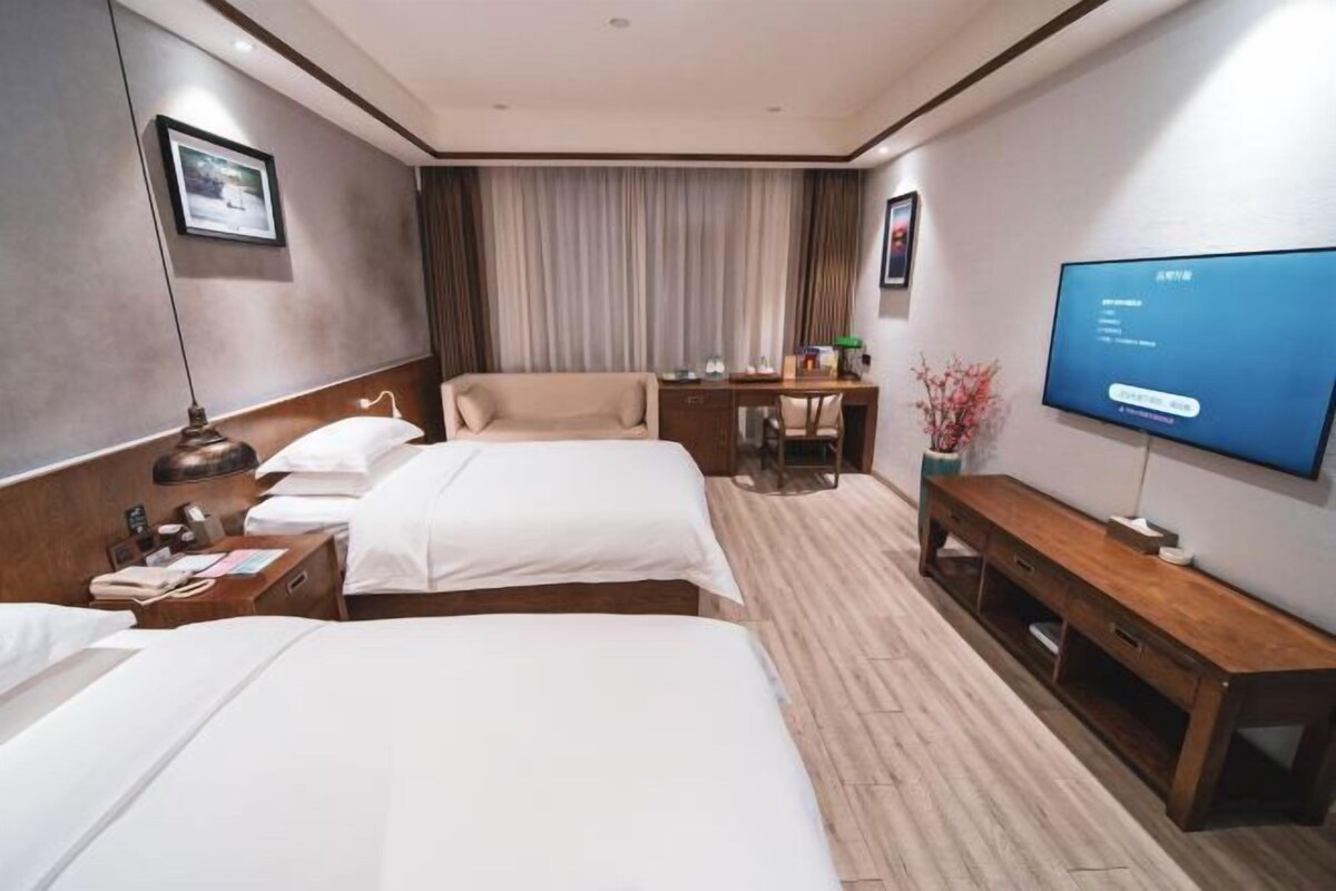 Quarto de hotel com duas camas, uma escrivaninha, televisão e uma janela grande com cortinas.