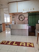 Uma área de recepção de hotel com parede de mármore, um relógio e uma porta verde.