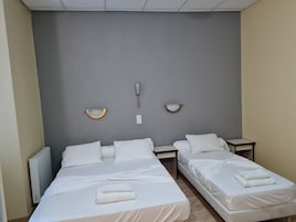 Quarto de hotel com duas camas de solteiro, mesa de cabeceira, telefone fixado na parede e radiador.