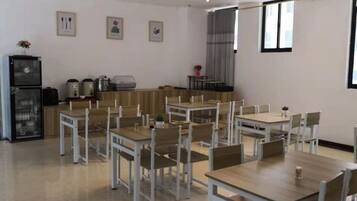 Uma sala de jantar com várias mesas e cadeiras, uma cozinha equipada e uma janela que proporciona luz natural.