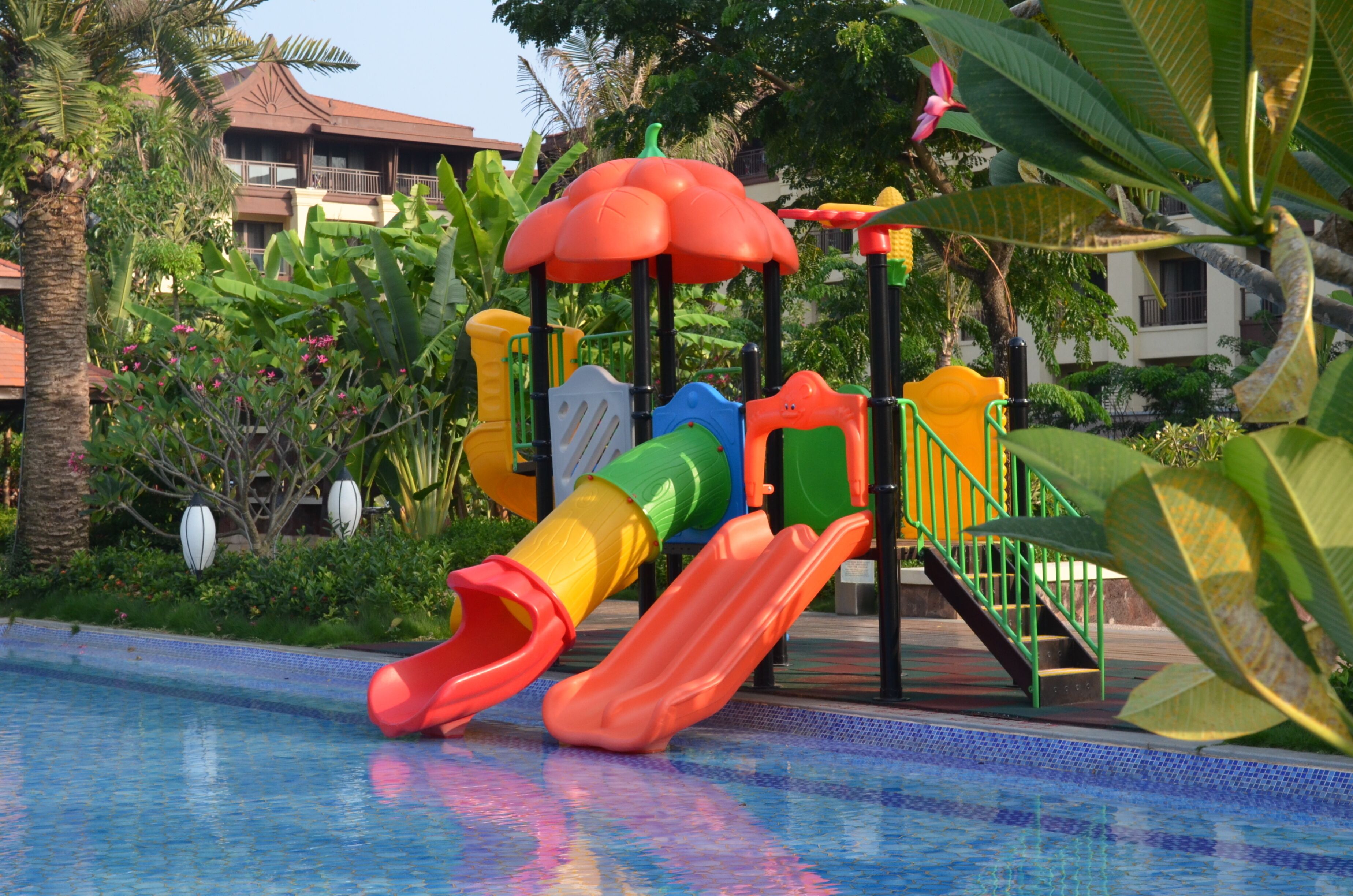 Espaço infantil com escorregadores e estrutura de escalada perto de uma piscina.