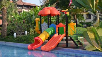 Espaço infantil com escorregadores e estrutura de escalada perto de uma piscina.