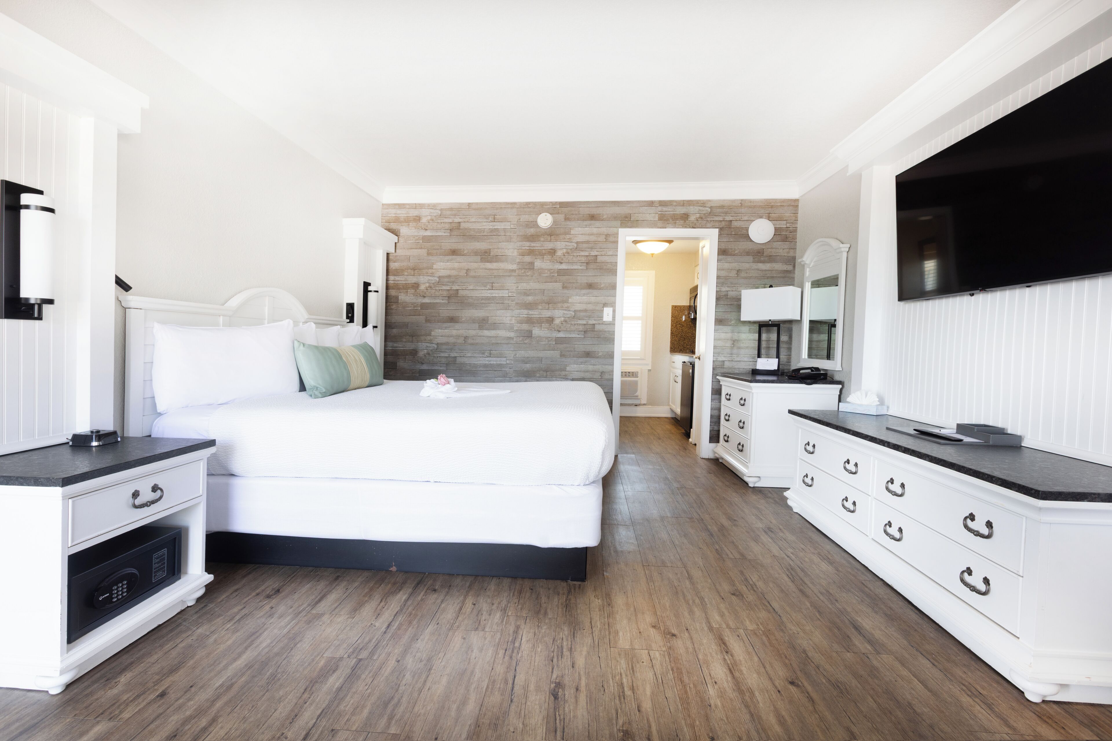 Quarto com cama, mesas de cabeceira, cômoda, televisão e parede de madeira.