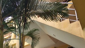 Um edifício com vários níveis, uma escadaria, palmeiras e uma parede exterior amarela.