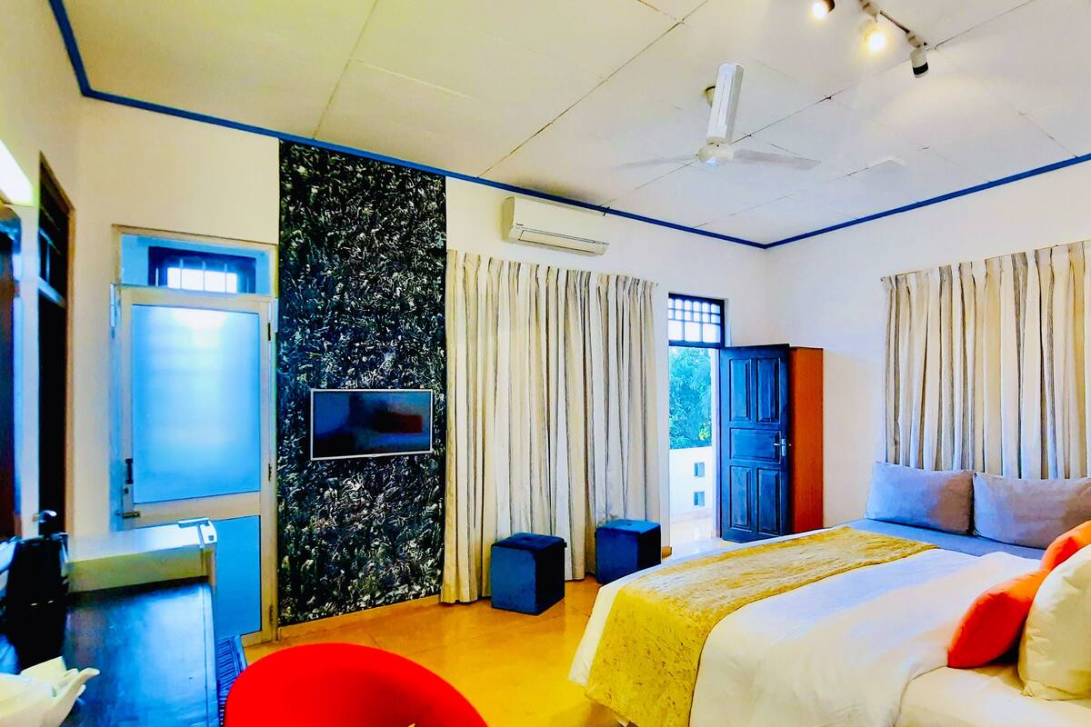 Quarto de hotel com cama, escrivaninha, televisão e janela com cortinas.
