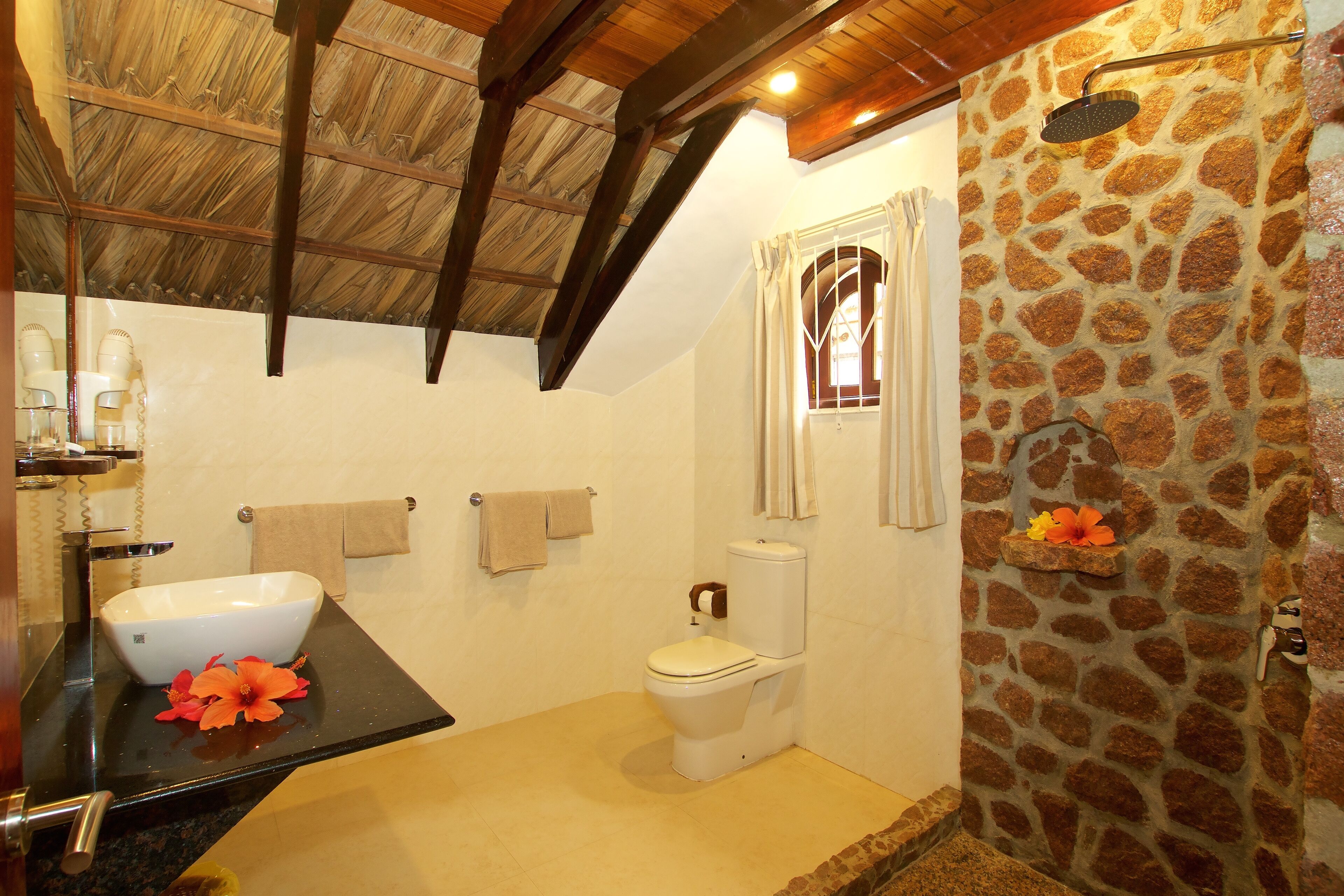 Casa de banho com parede de pedra, lavatório branco, sanita e chuveiro.