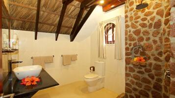 Casa de banho com parede de pedra, lavatório branco, sanita e chuveiro.