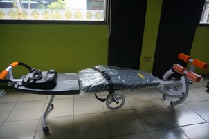 Mesa de exames médicos com apoio para os pés e uma cadeira de massagem em um quarto com paredes verdes e uma janela.