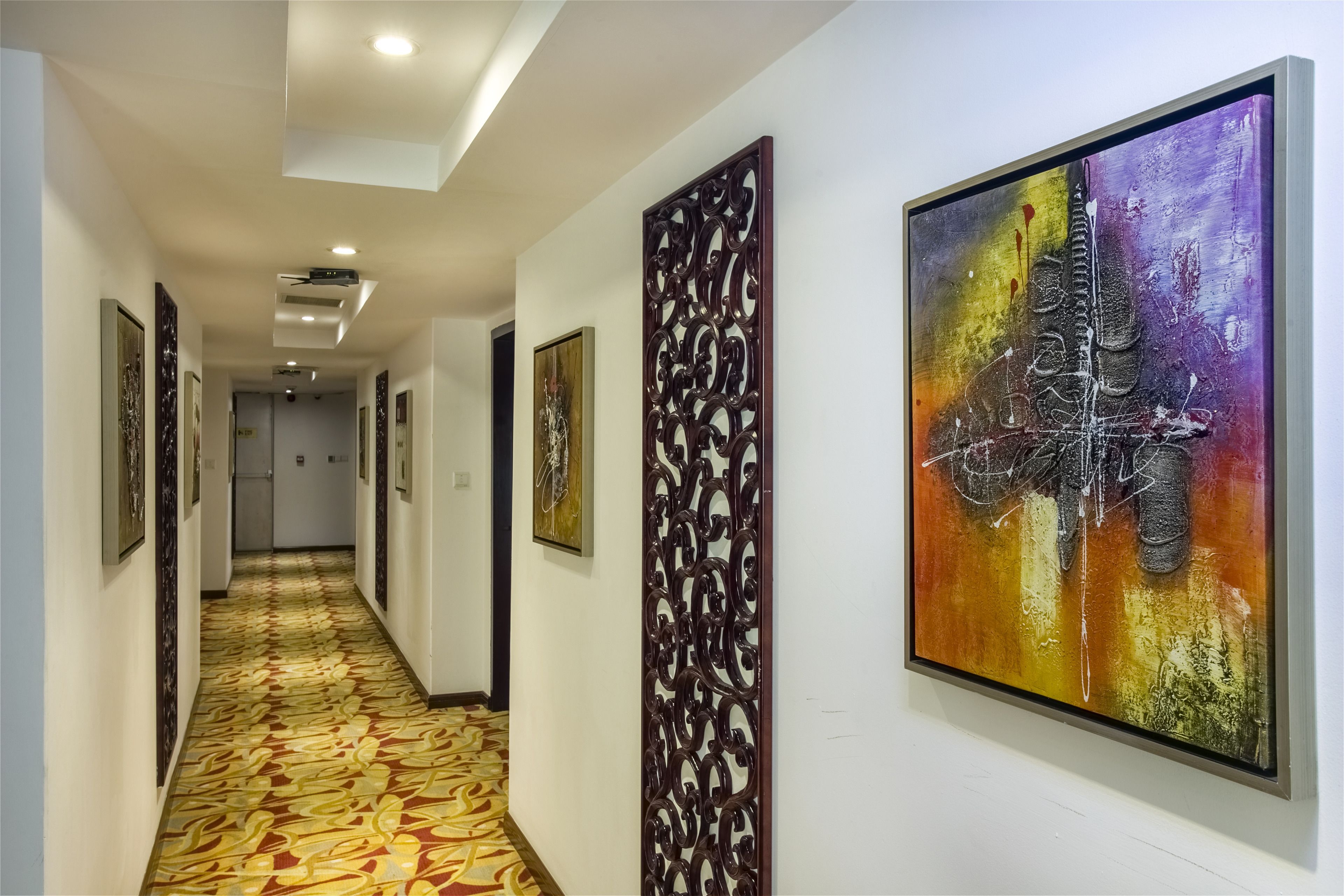 Um corredor com carpete estampado, quadros nas paredes e um painel decorativo.