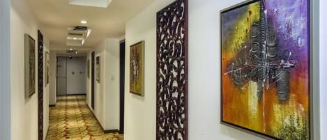 Um corredor com carpete estampado, quadros nas paredes e um painel decorativo.