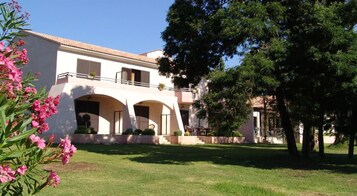 Um edifício de dois andares com teto plano, varanda no andar superior e um pátio coberto com escada que leva à entrada.