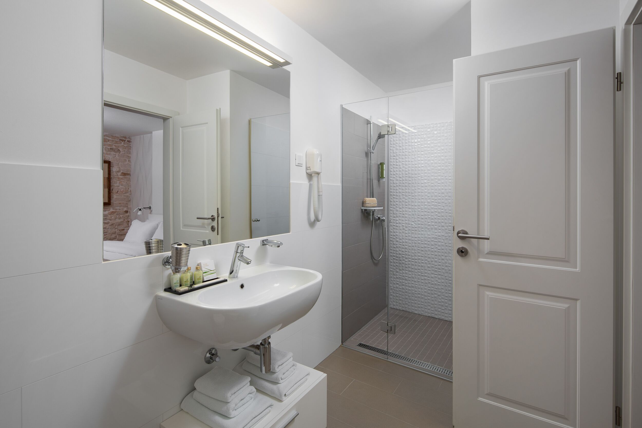 Uma casa de banho moderna com lavatório branco, espelho e chuveiro.