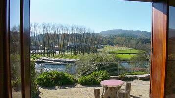 Vista de um quarto com uma janela grande que dá para uma área ajardinada com árvores, um campo gramado e um corpo d'água.