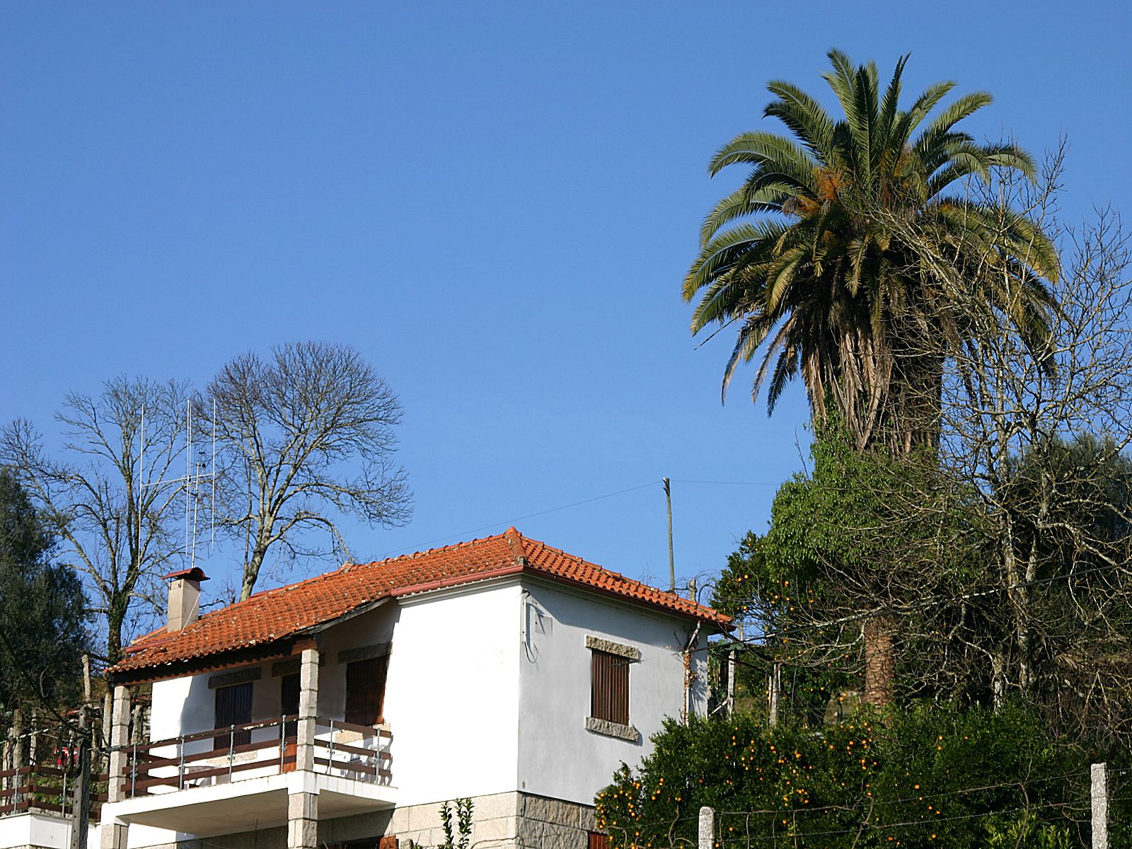 Um edifício de dois andares com telhado de telhas vermelhas, uma varanda e fachada branca.