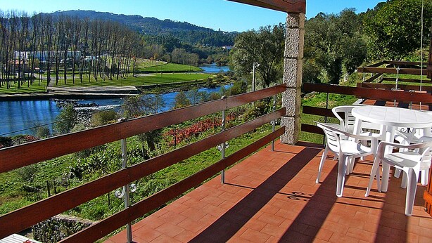 Uma varanda com vista para um rio, rodeada por vegetação e colinas.