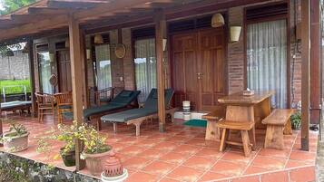 Uma área externa coberta com mobiliário de madeira, incluindo cadeiras de estar e uma mesa, e plantas em vasos.