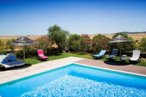Uma piscina com espreguiçadeiras e guarda-sóis, cercada por vegetação e colinas ao fundo.