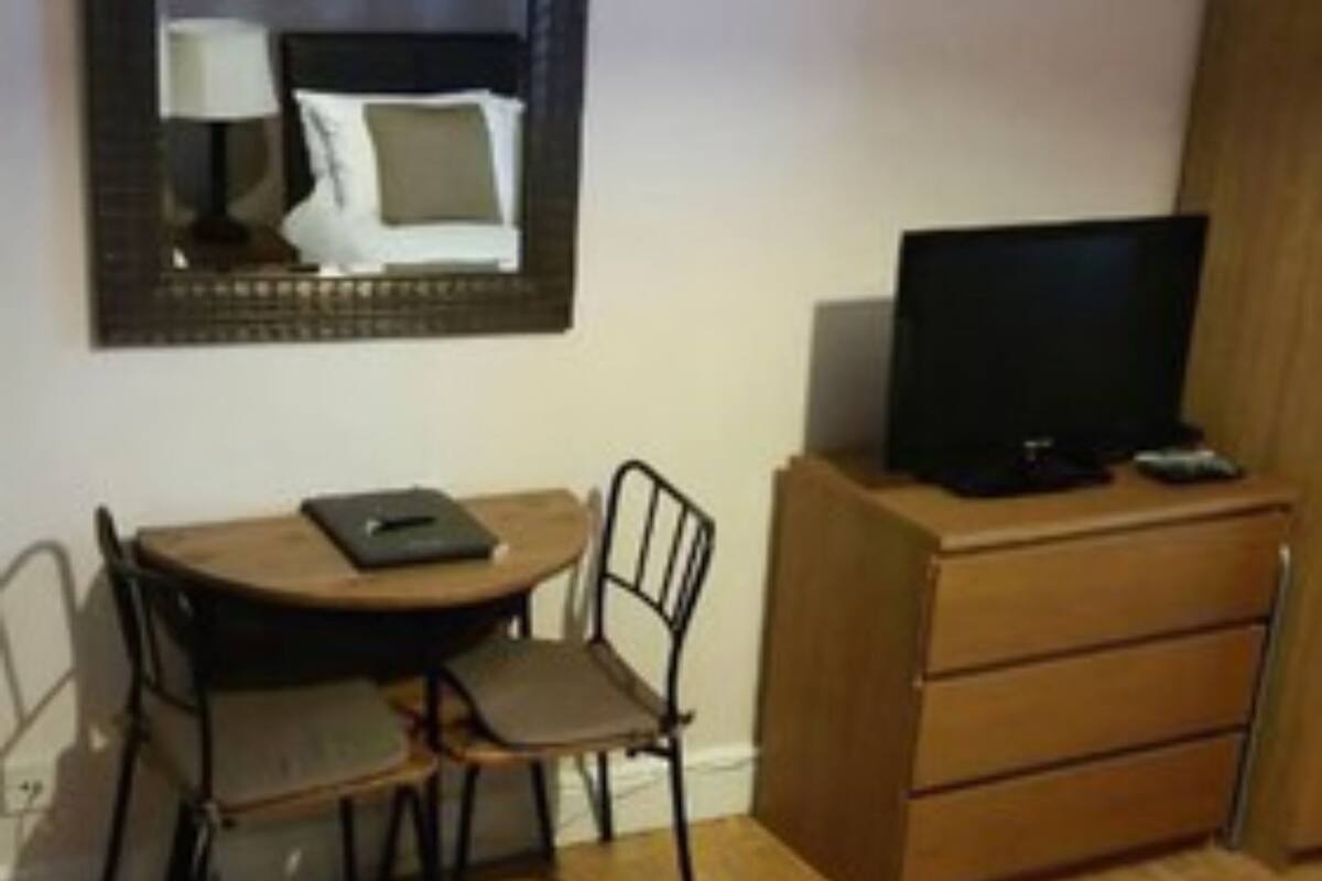 Quarto de hotel com cama, escrivaninha com cadeira, televisão sobre um móvel de madeira e espelho na parede.