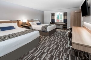 Quarto de hotel com duas camas, uma escrivaninha, uma cadeira, uma televisão e janela com cortinas.