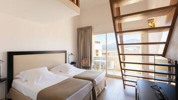 Quarto de hotel com duas camas, uma escrivaninha com computador, uma cadeira, um abajur e vista para o exterior.