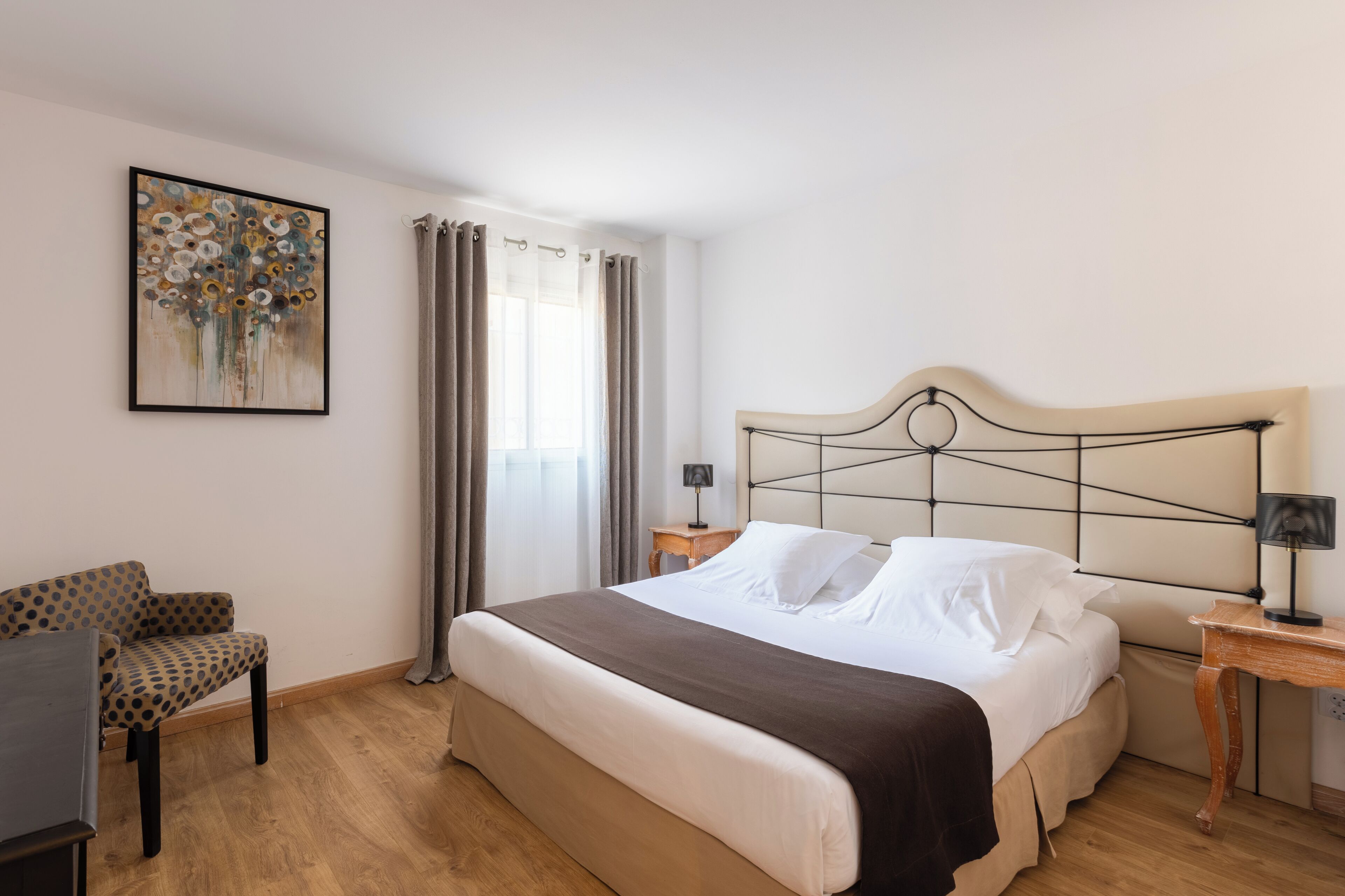 Quarto bem arrumado com cama, cadeira, mesa de cabeceira e um quadro na parede.