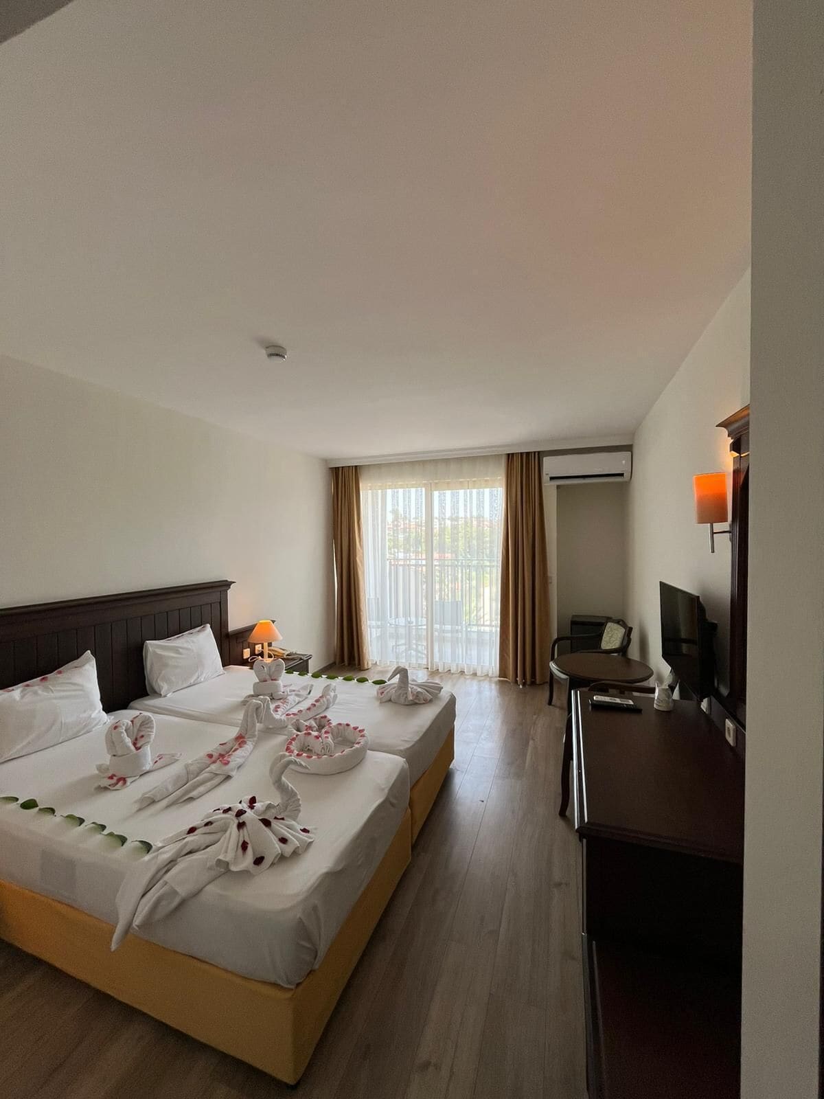 Quarto de hotel com duas camas, uma escrivaninha, uma cadeira, ar condicionado e televisão.