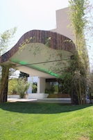 Um edifício moderno com estrutura de telhado curva, rodeado por plantas de bambu e um gramado bem cuidado.