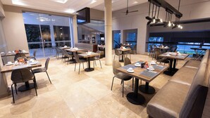 Um restaurante moderno com tetos altos, amplas janelas e diversas opções de assentos, incluindo mesas e bancos.