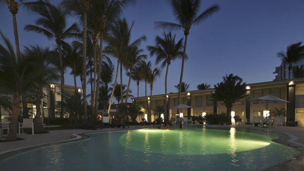 Uma piscina rodeada por palmeiras e edifícios de hotel ao entardecer.