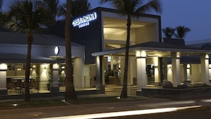 Um hotel moderno com uma placa visível, área de estar ao ar livre e palmeiras.