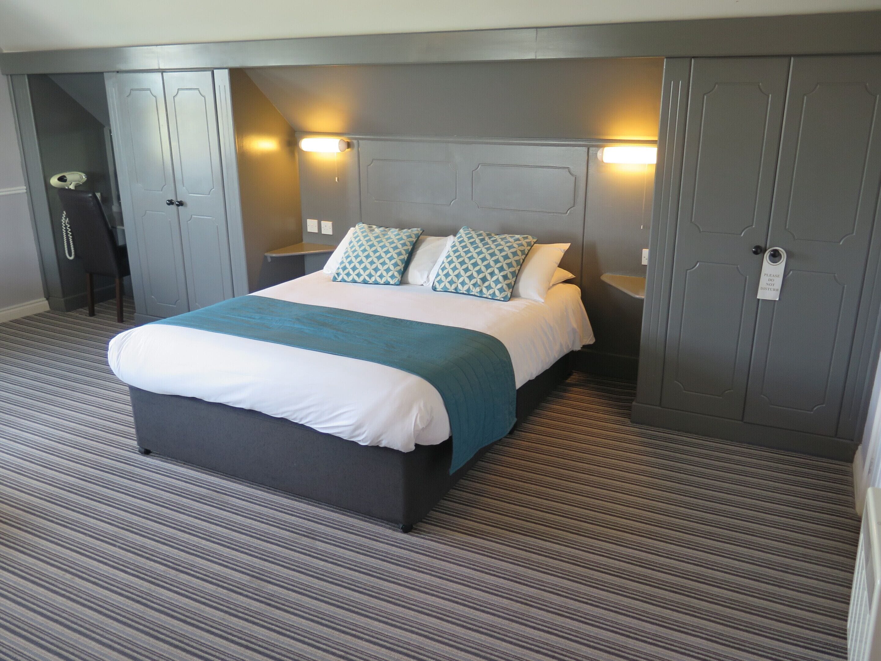 Quarto de hotel com uma cama grande, paredes cinzentas e um tapete riscado.