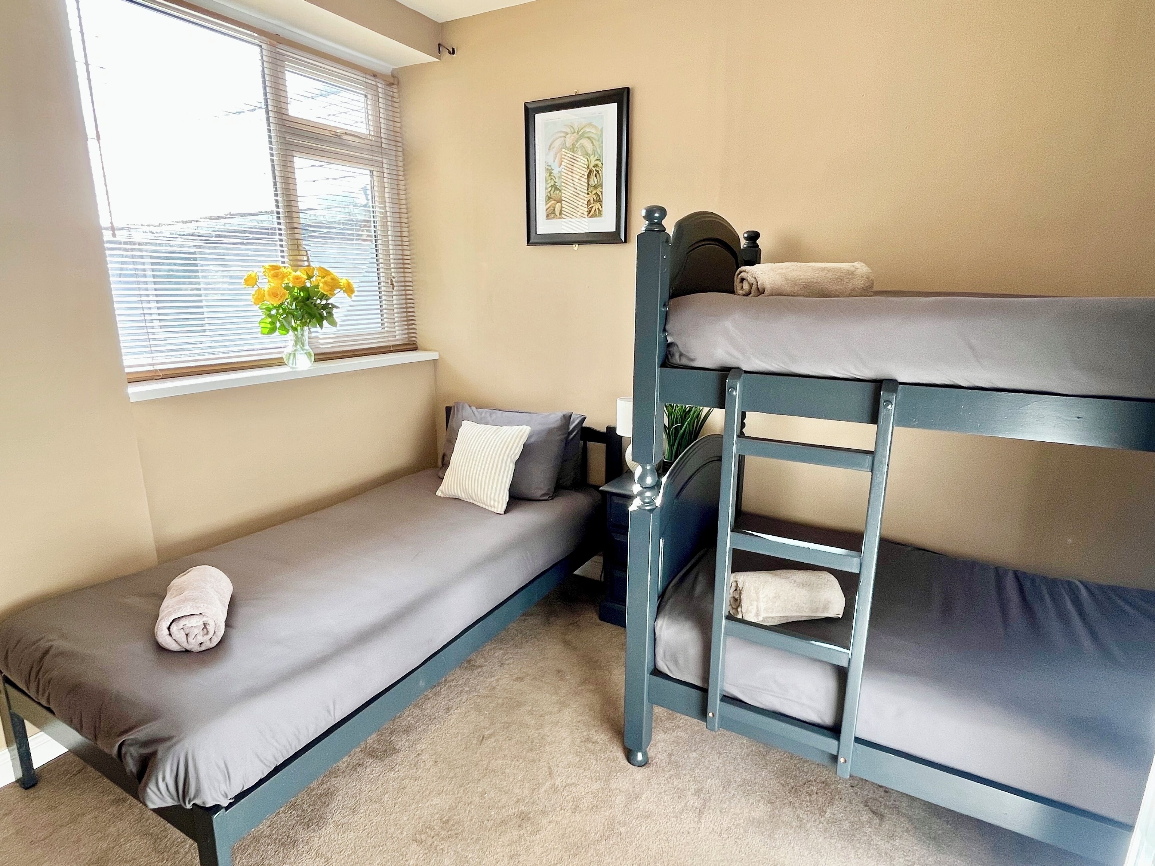 Quarto com beliche, janela, quadro emoldurado e vaso com flores.
