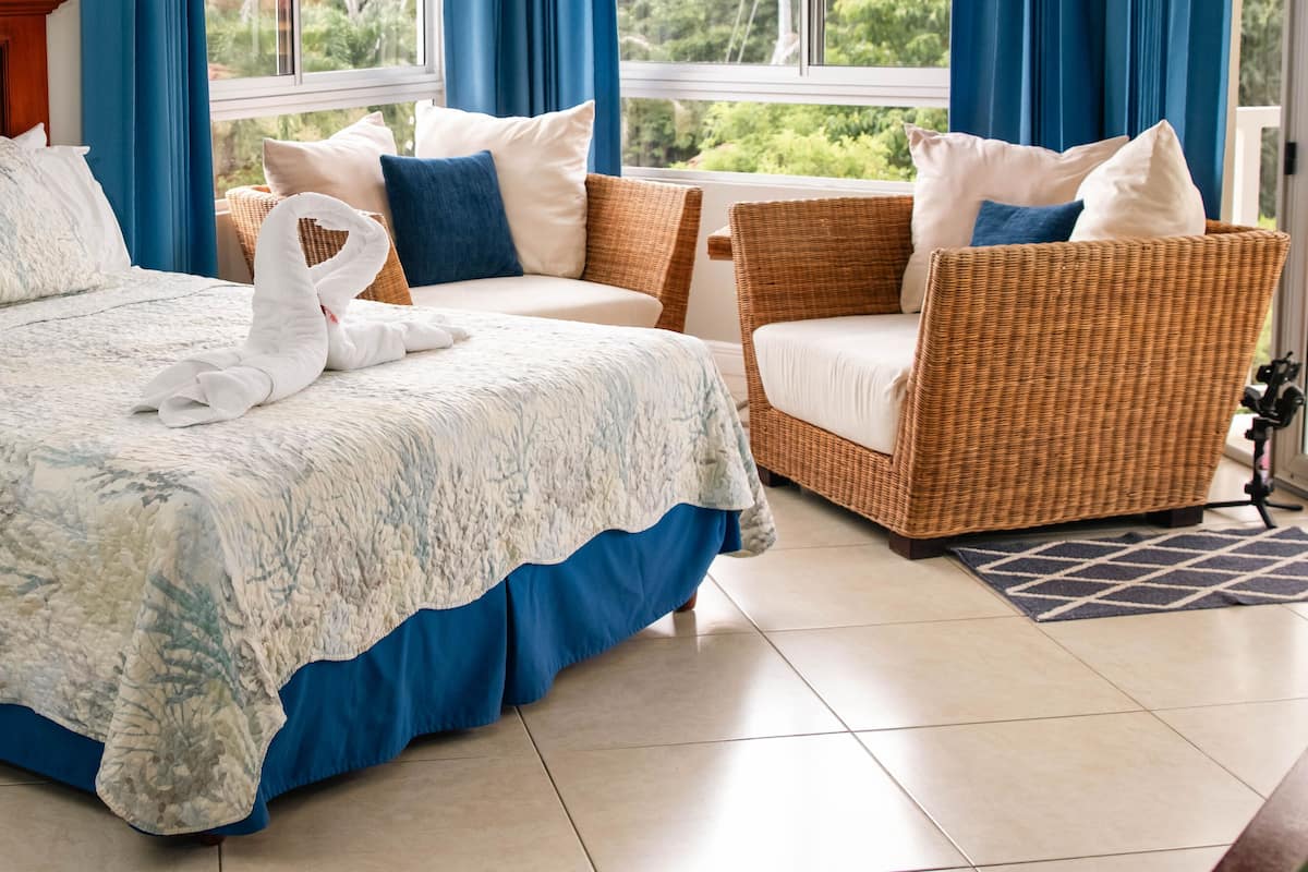 Uma cama bem arrumada com colcha floral azul e branca, cabeceira de madeira e toalha branca dobrada sobre a cama.