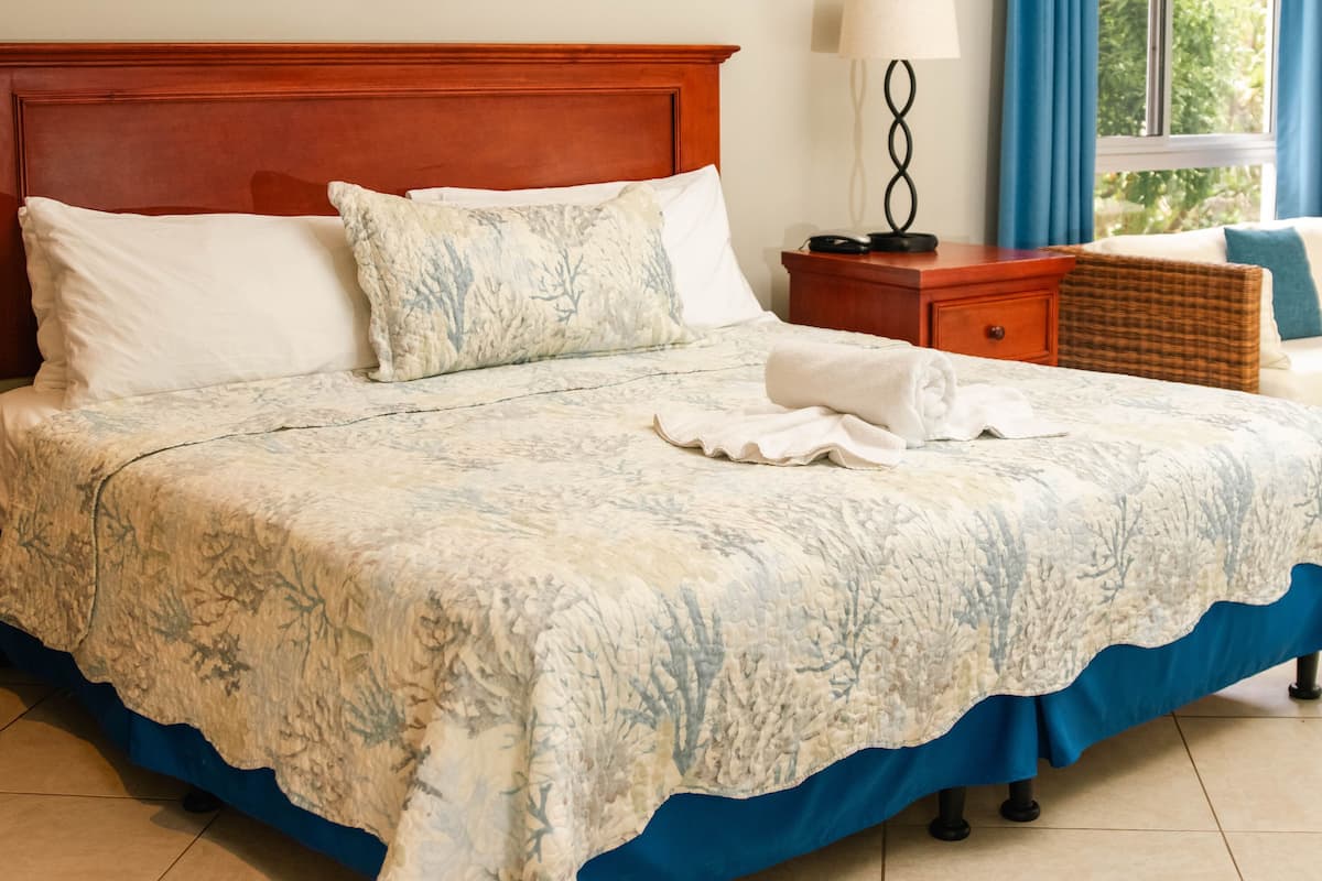 Cama bem arrumada com colcha floral azul e branca, cabeceira de madeira e travesseiro branco.