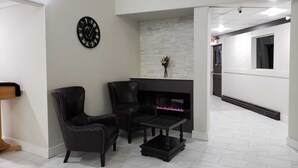 Um lobby moderno com lareira, duas poltronas de couro, uma mesa pequena e um relógio na parede.