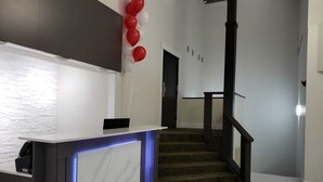 Uma área de recepção com um balcão branco, uma escada com corrimão preto e uma parede decorada com balões vermelhos e brancos.