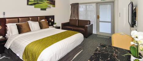 Quarto de hotel com uma cama grande, um sofá, uma mesa de jantar e uma televisão.