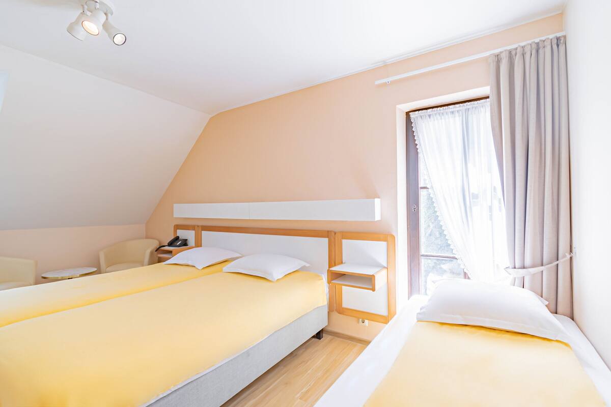 Quarto de hotel com uma cama grande, uma cama menor, uma escrivaninha e uma cadeira.