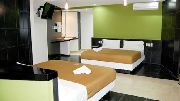 Quarto de hotel com duas camas, uma escrivaninha, uma televisão e uma parede verde.
