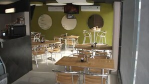 Uma sala de jantar com várias mesas e cadeiras, uma televisão e uma cozinha equipada.