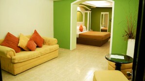 Quarto com sofá amarelo, uma pequena mesa redonda e uma cama ao fundo.