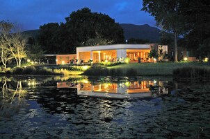 Um hotel moderno com piscina e área externa para sentar, rodeado por árvores e uma montanha ao fundo.