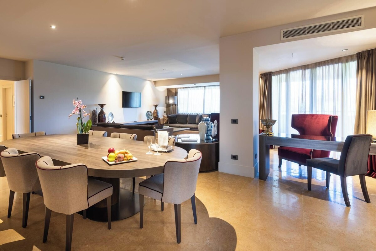 Quarto de hotel moderno com área de jantar, sala de estar e vista para a cidade.