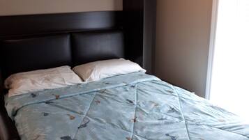 Uma cama com cabeceira escura, um edredom azul claro com estampas de pássaros e um travesseiro branco.