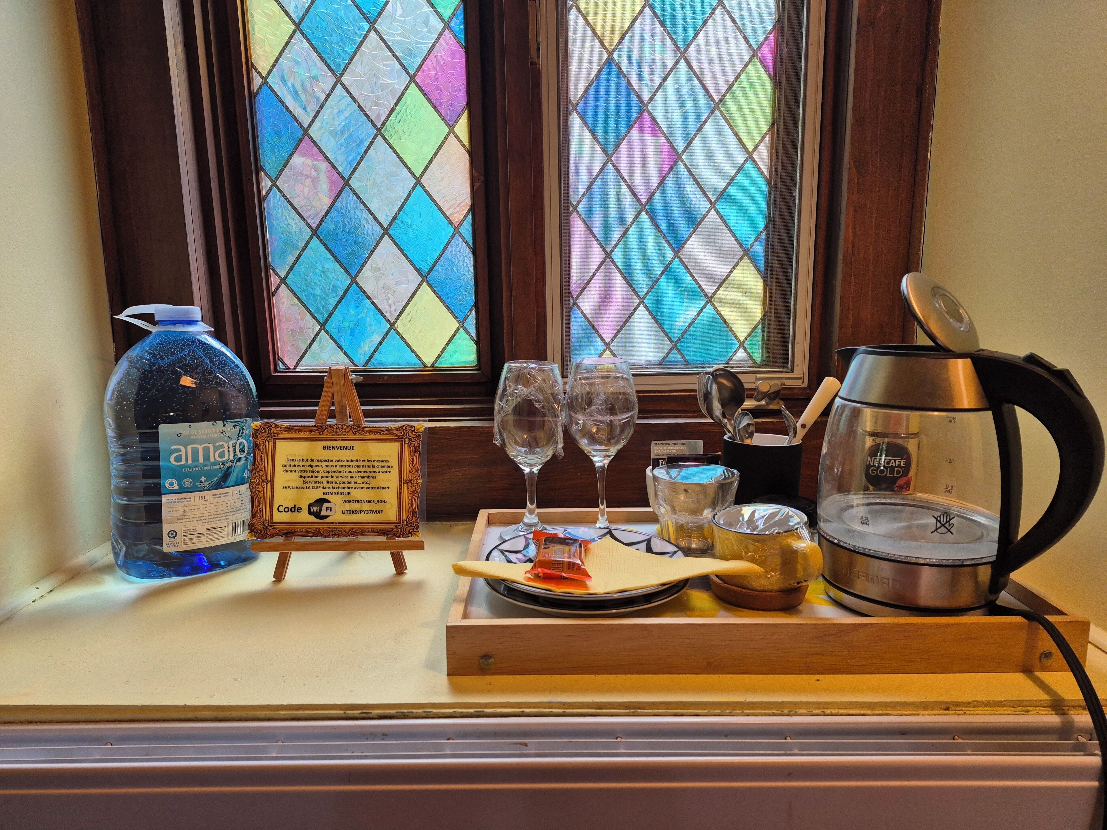 Um minibar com uma garrafa de água, copos de vinho, uma cafeteira e um tabuleiro.