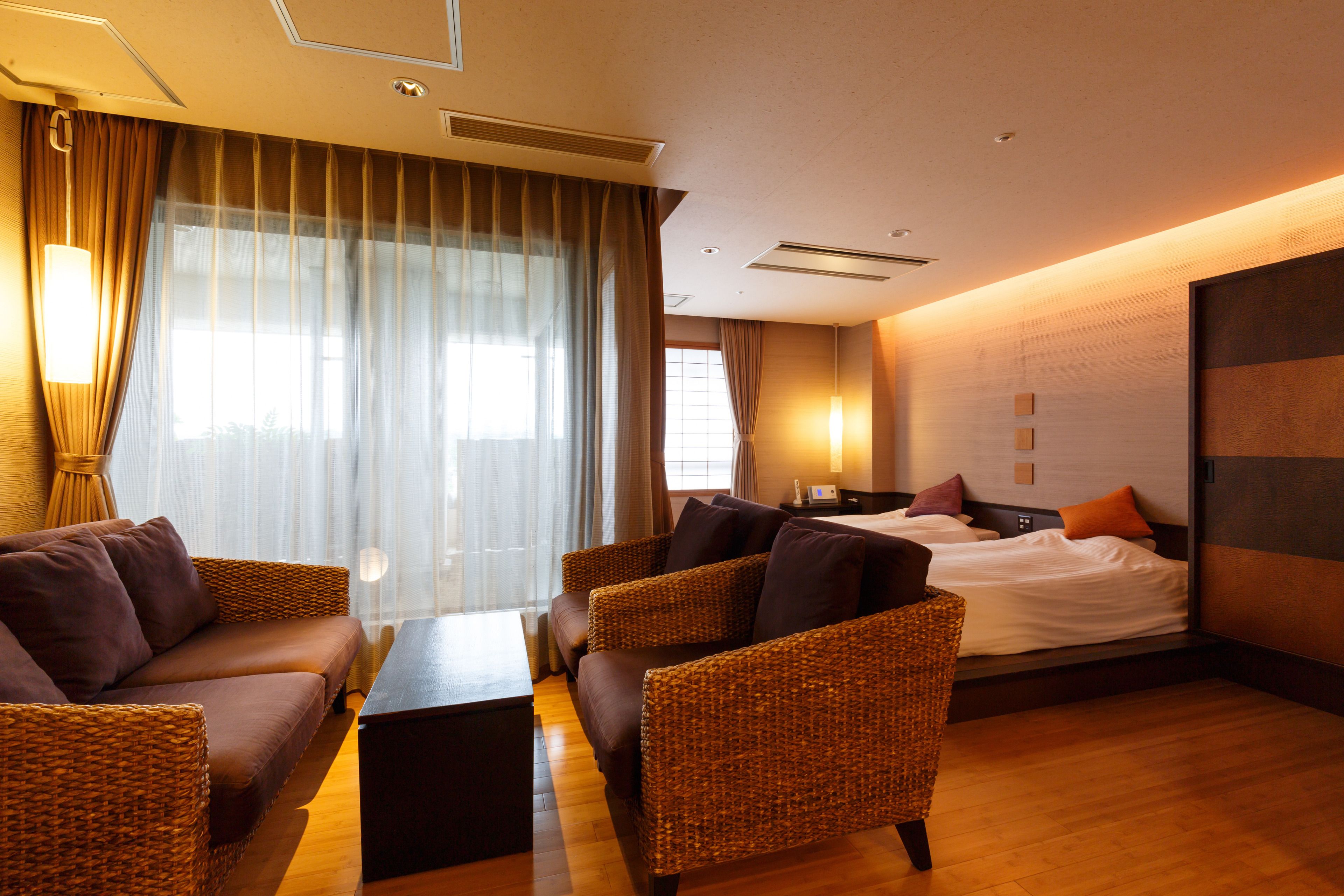 Quarto de hotel com cama, dois sofás, mesa de centro e uma janela grande com cortinas.