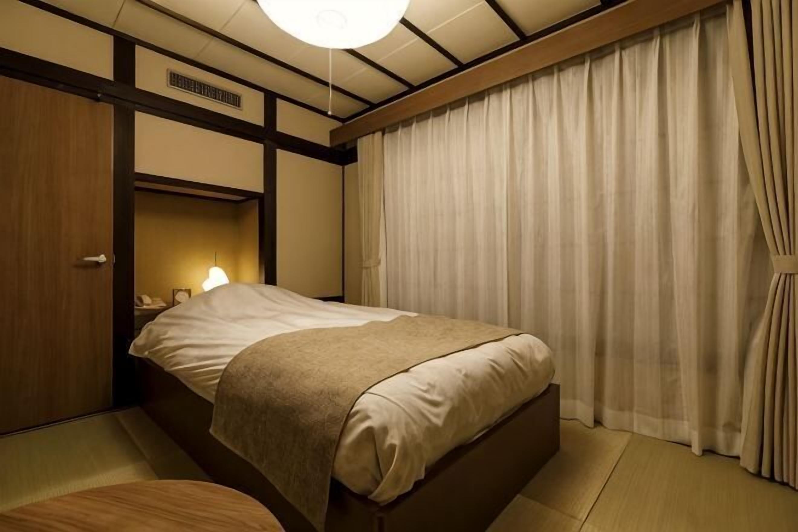 Um quarto com uma cama, uma mesa de cabeceira, uma luminária e uma janela com cortinas.