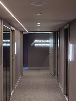 Um corredor moderno com piso coberto por carpete, iluminação embutida no teto e uma placa fixada na parede.